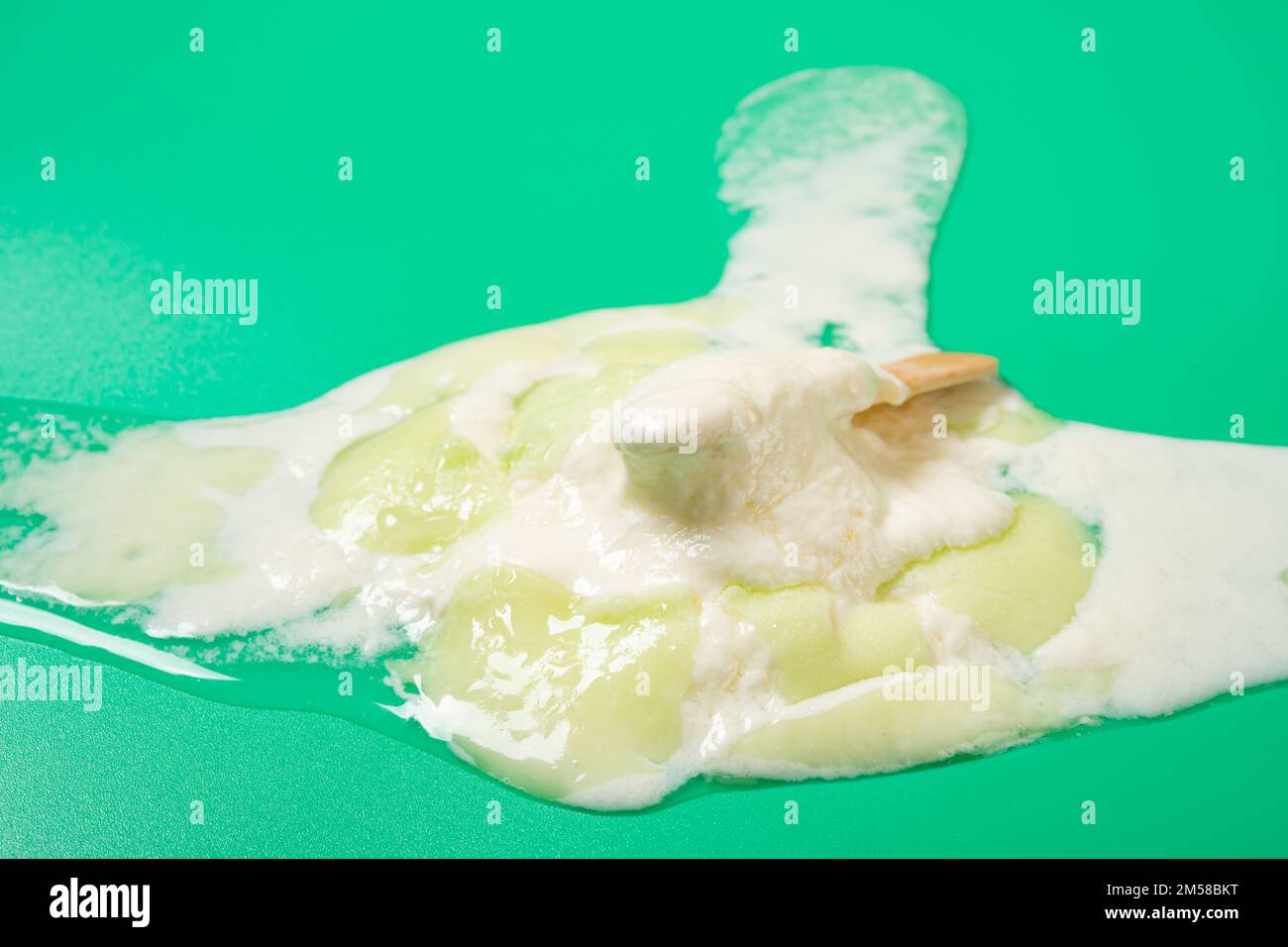 mostly melted green apple shape and flavor popsice on green background ...