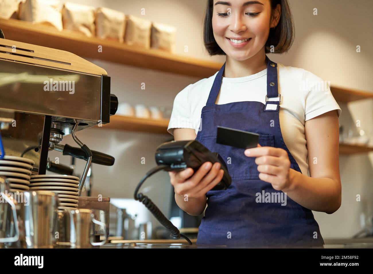 Beautiful smiling asian girl, barista insert client credit card in POS ...