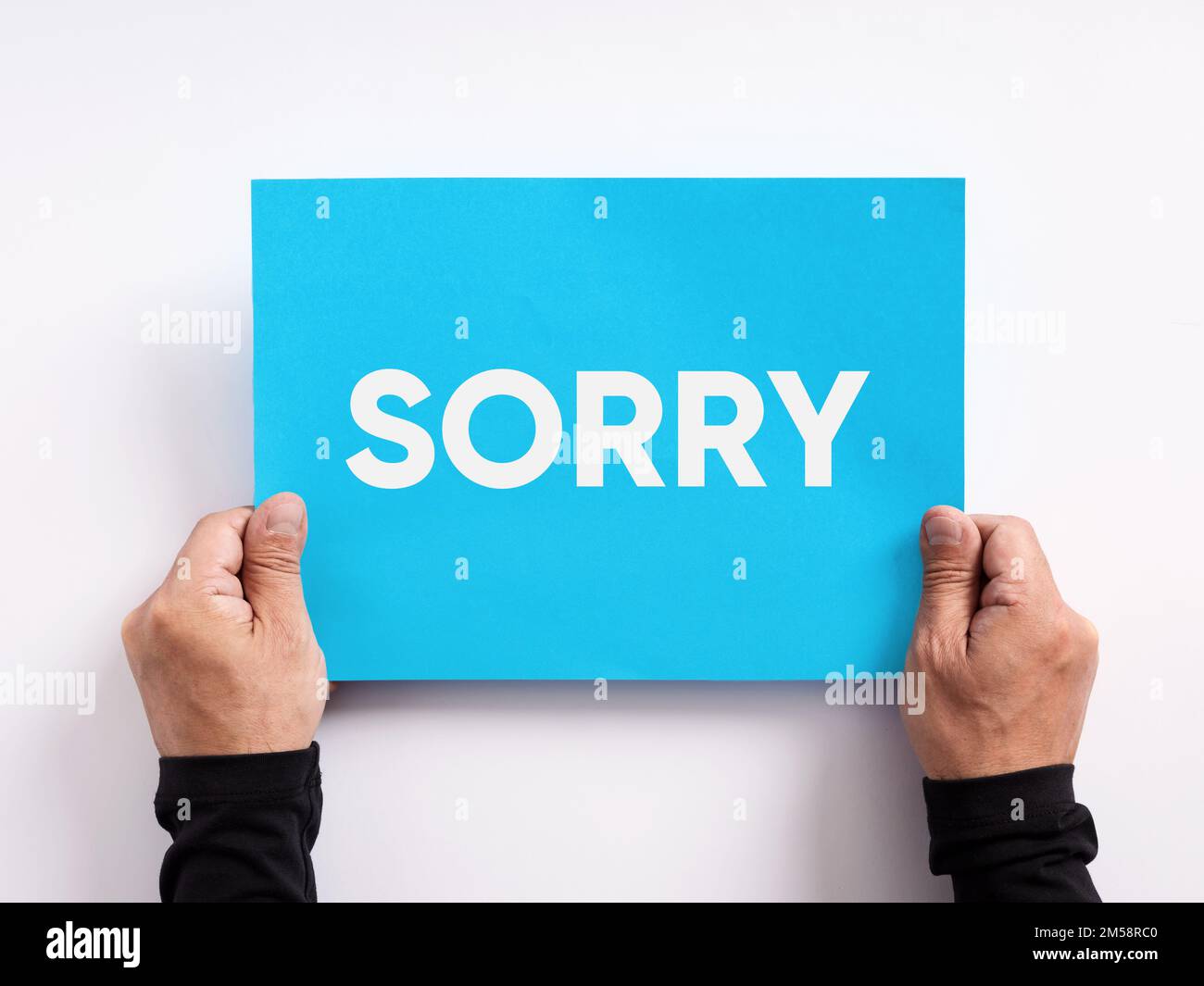 Male hand holding a blue paper with the message sorry Stock Photo - Alamy