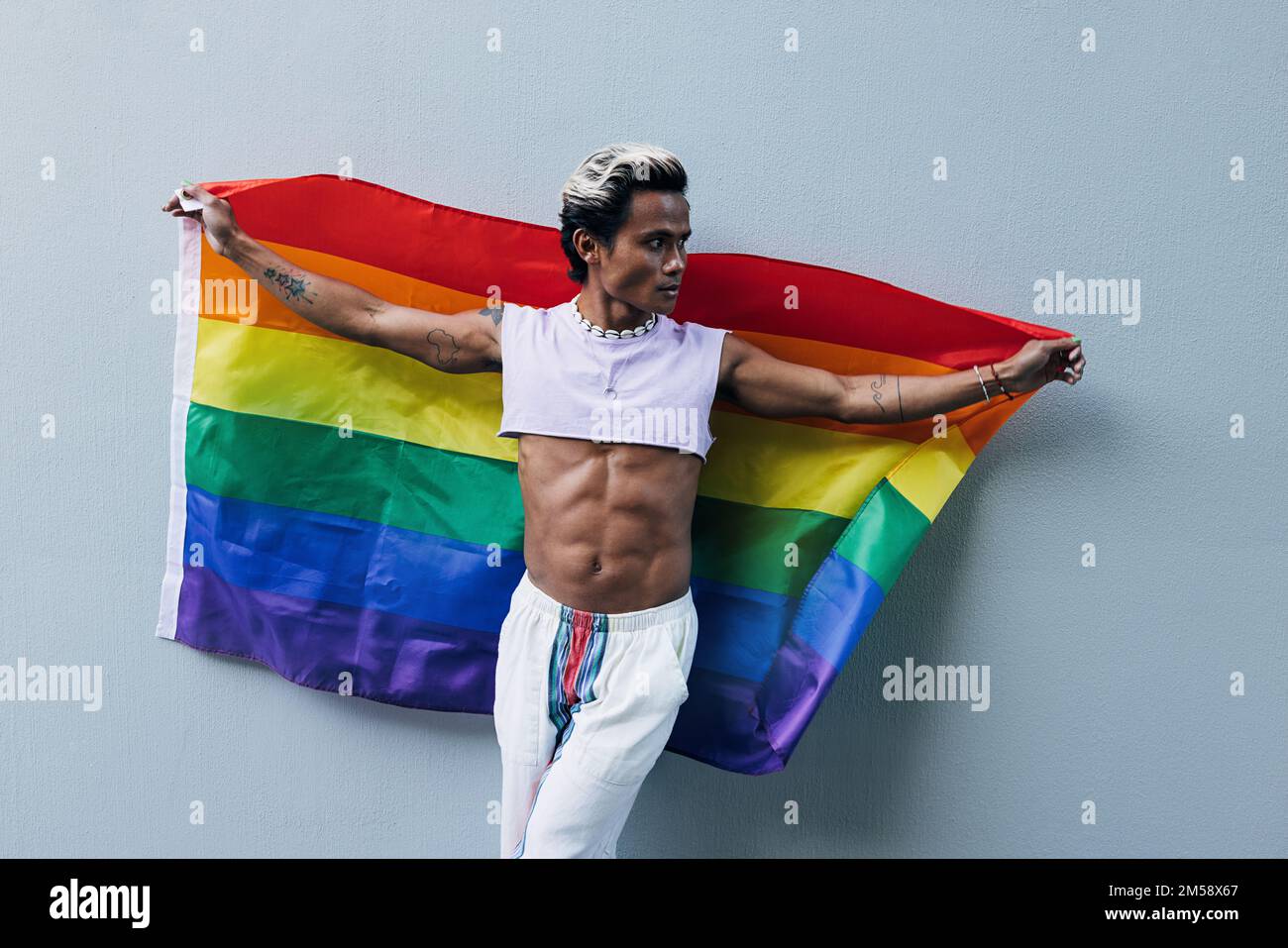 Muscular stylish guy holding an LGBT rainbow flag at a grey wall Stock ...