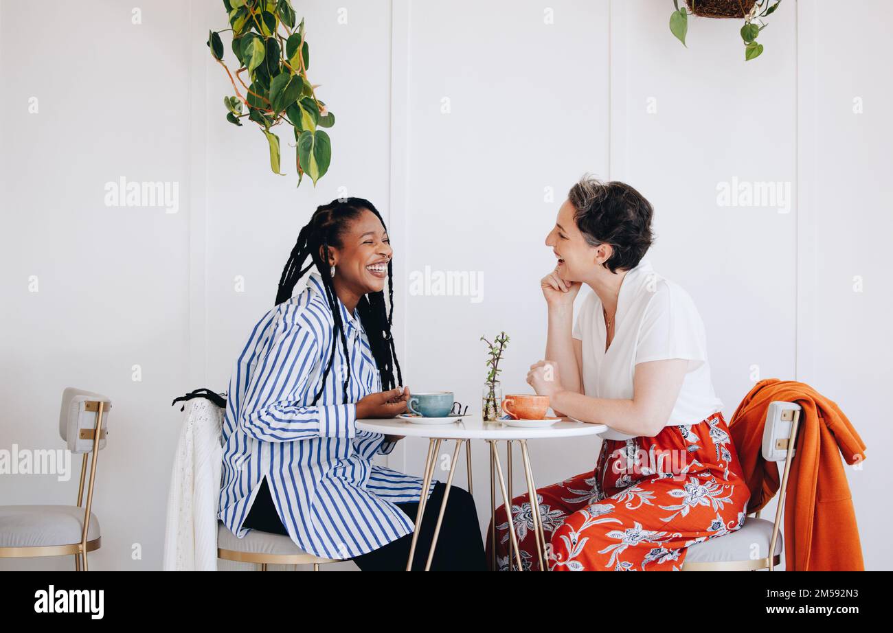 Two happy businesswomen chatting and laughing together during a coffee ...