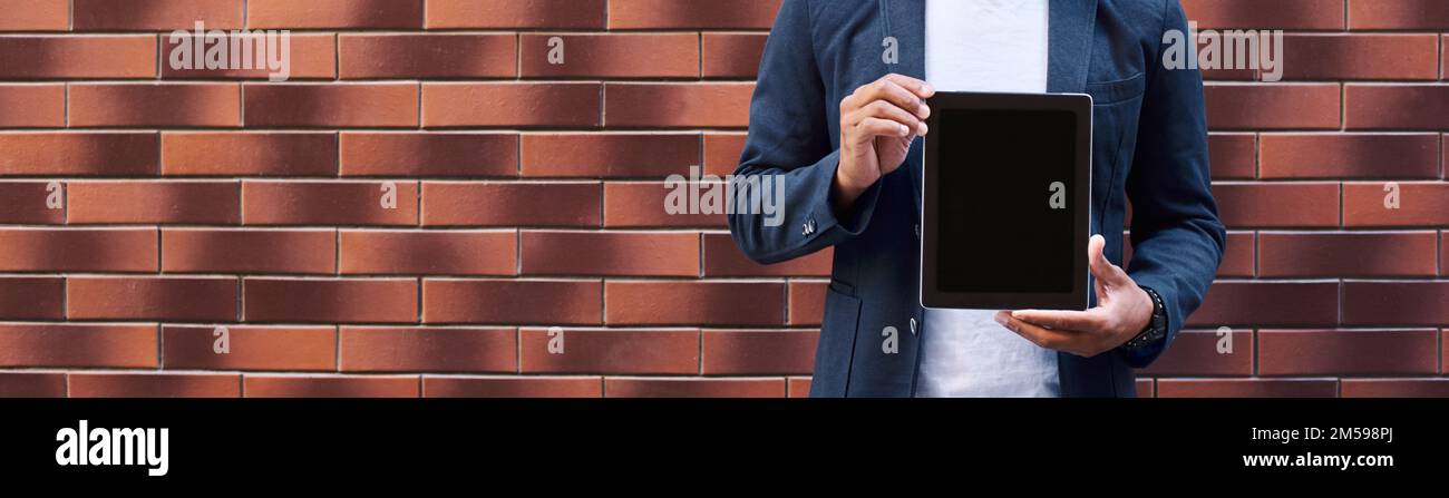 Promotion. Young guy standing on wall showing screen of digital tablet ...