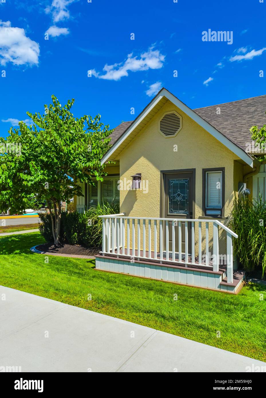 Small yellow family house on sunny day with green lawn and concrete ...