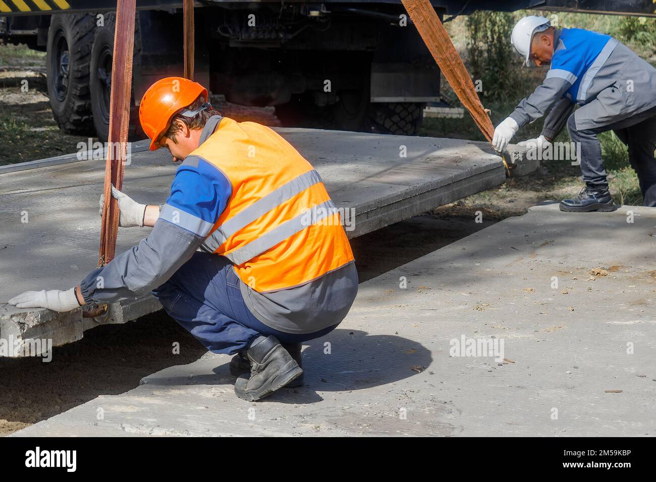 Slinger lays concrete slab on construction site on summer day. Worker ...