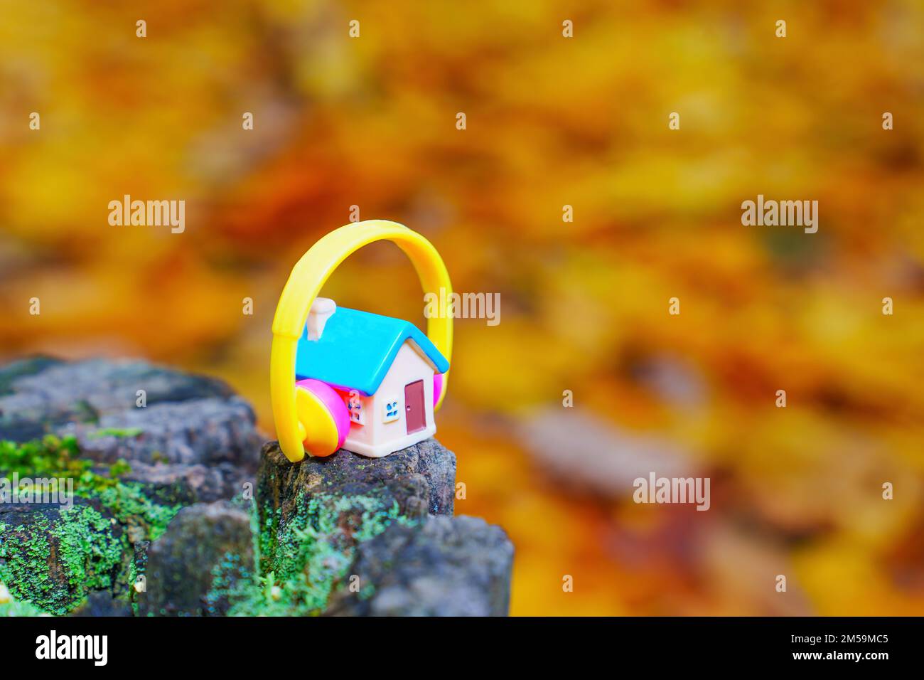 Colorful toy house with soundproofing earmuffs placed on a tree stump ...