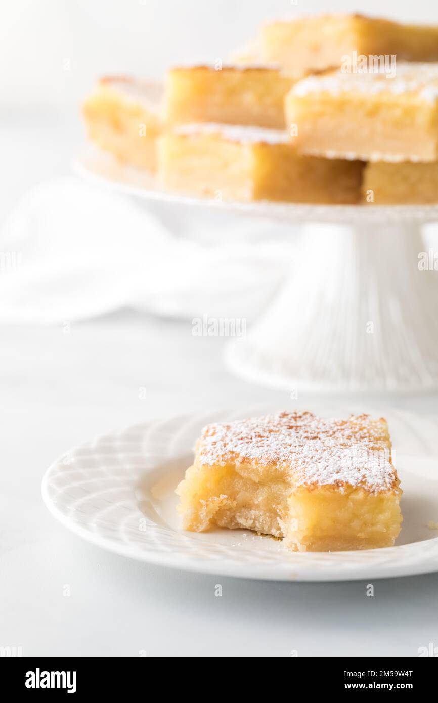 A lemon square with a bite out, with more on a dessert stand in behind ...