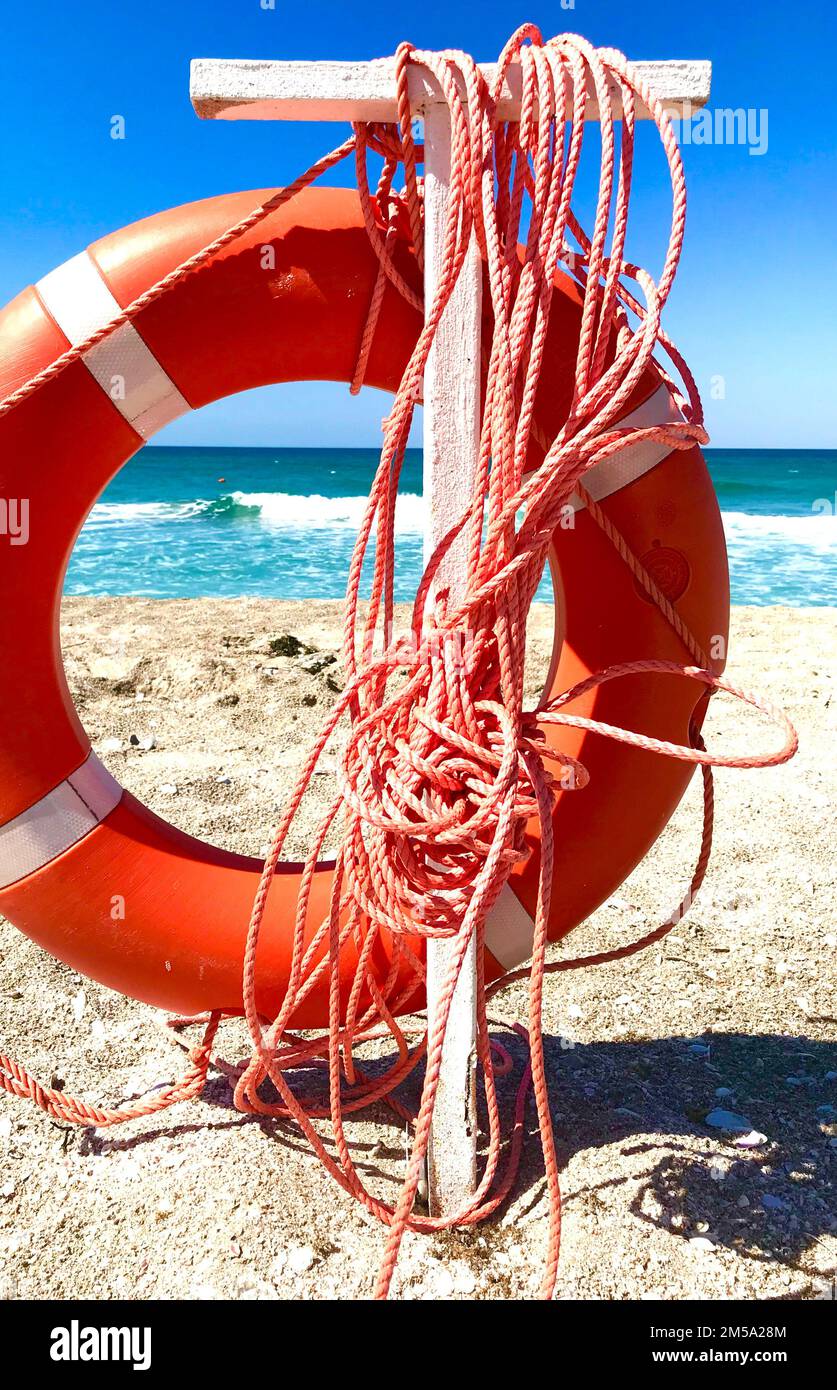 Orange lifebuoy and rope ropes on the sandy sea beach. Ocean safety ...