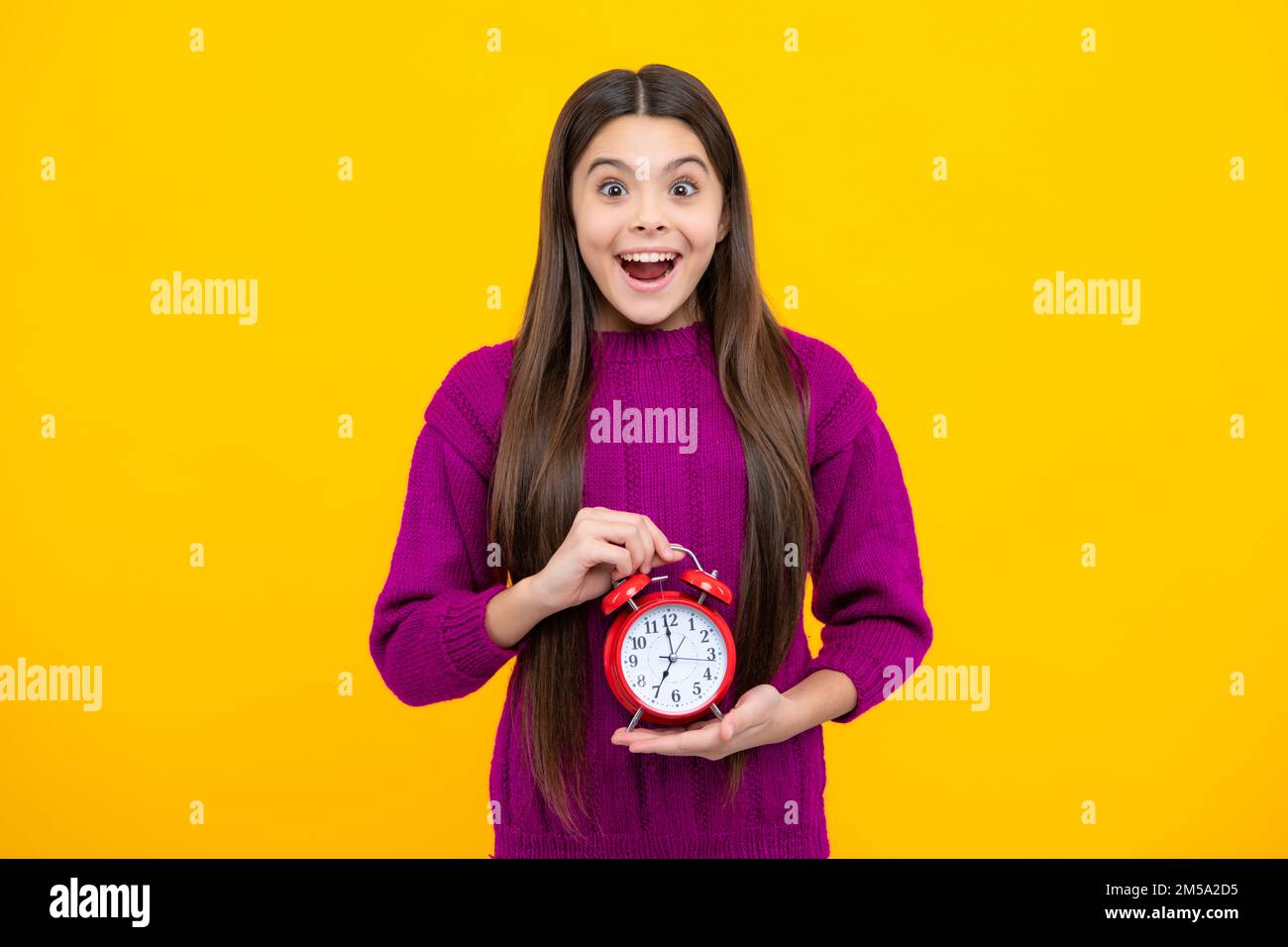 Excited face. Teen girl holding clock over yellow background. Early ...