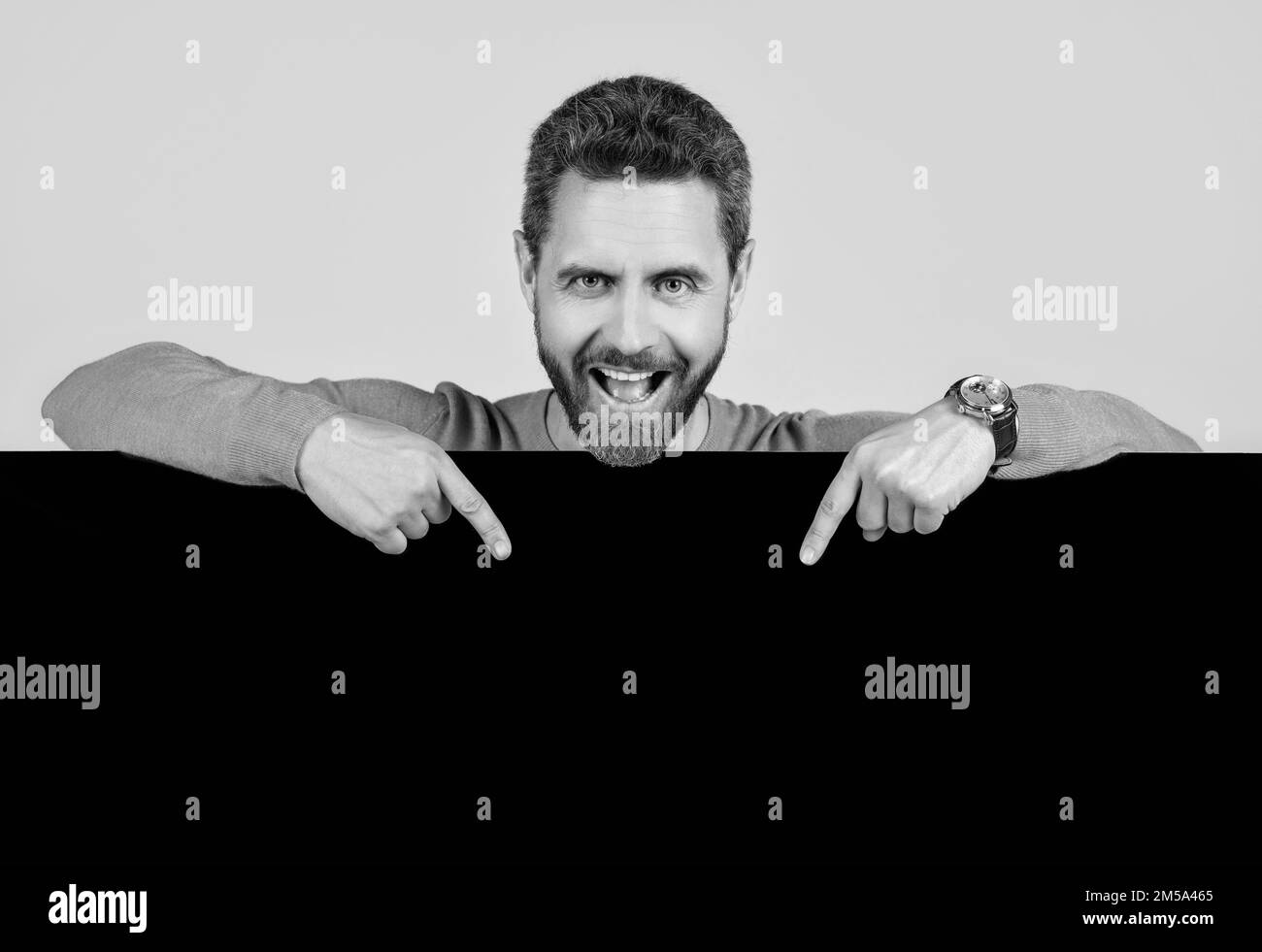 happy bearded man pointing finger on blank black paper banner with copy ...