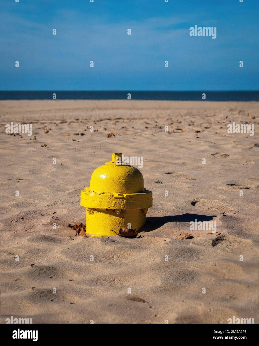 A vertical shot of a yellow fire hydrant in the sand at a beach shore ...