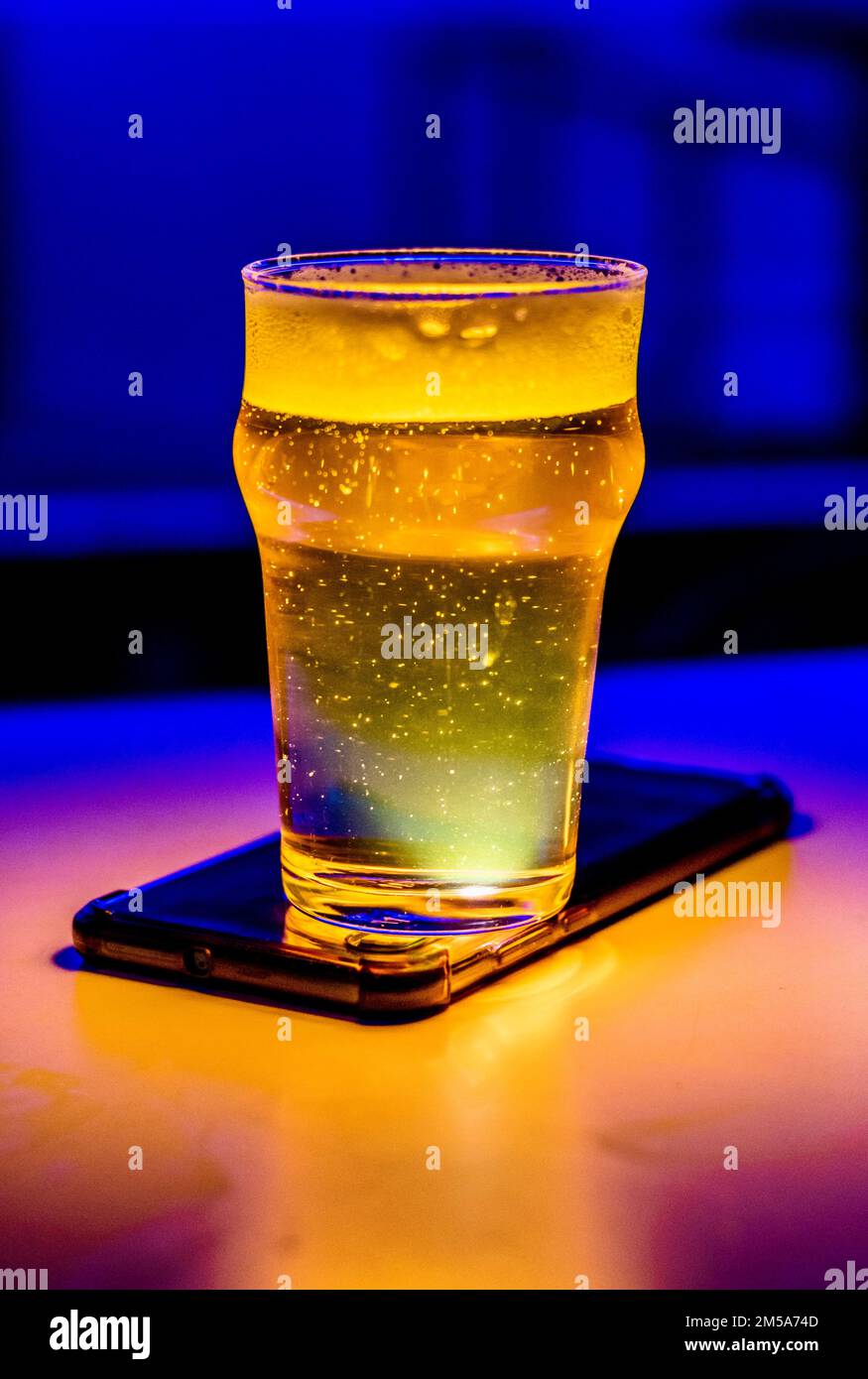 Freshly tapped glass of beer over the flash of a mobile phone. Light ...