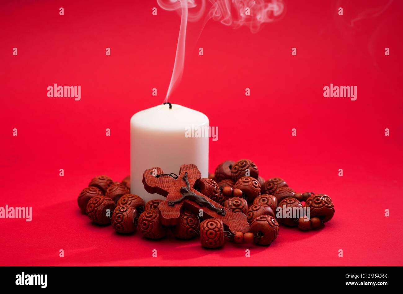 red wooden catholic rosary with white extinguished candle with smoke ...
