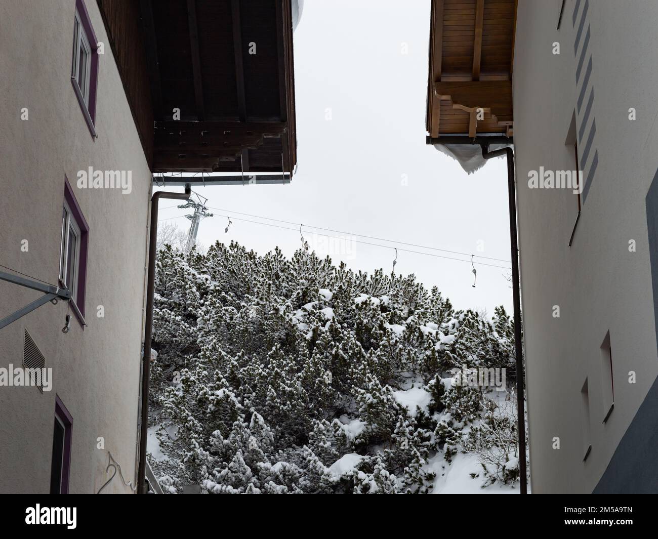 Ski lift and snowy bushes between big houses. Building exteriors on the ...