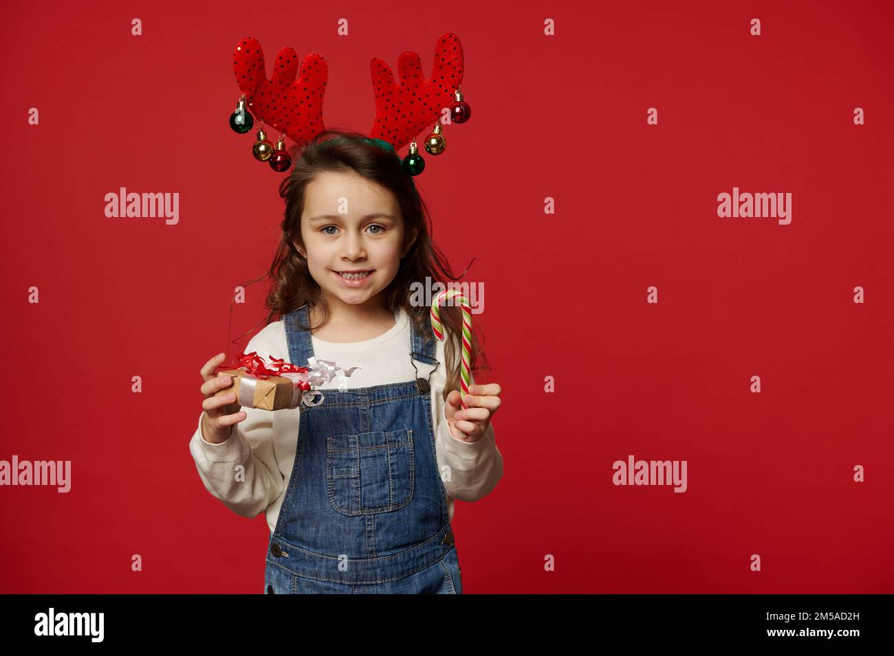 Lovely little girl wearing deer antler hoop, smiles posing with candy ...