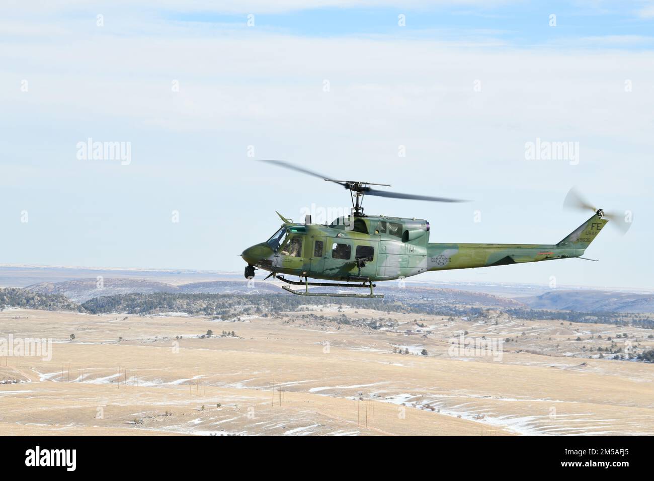 A helicopter from the 37th Helicopter Squadron flies over fields and ...