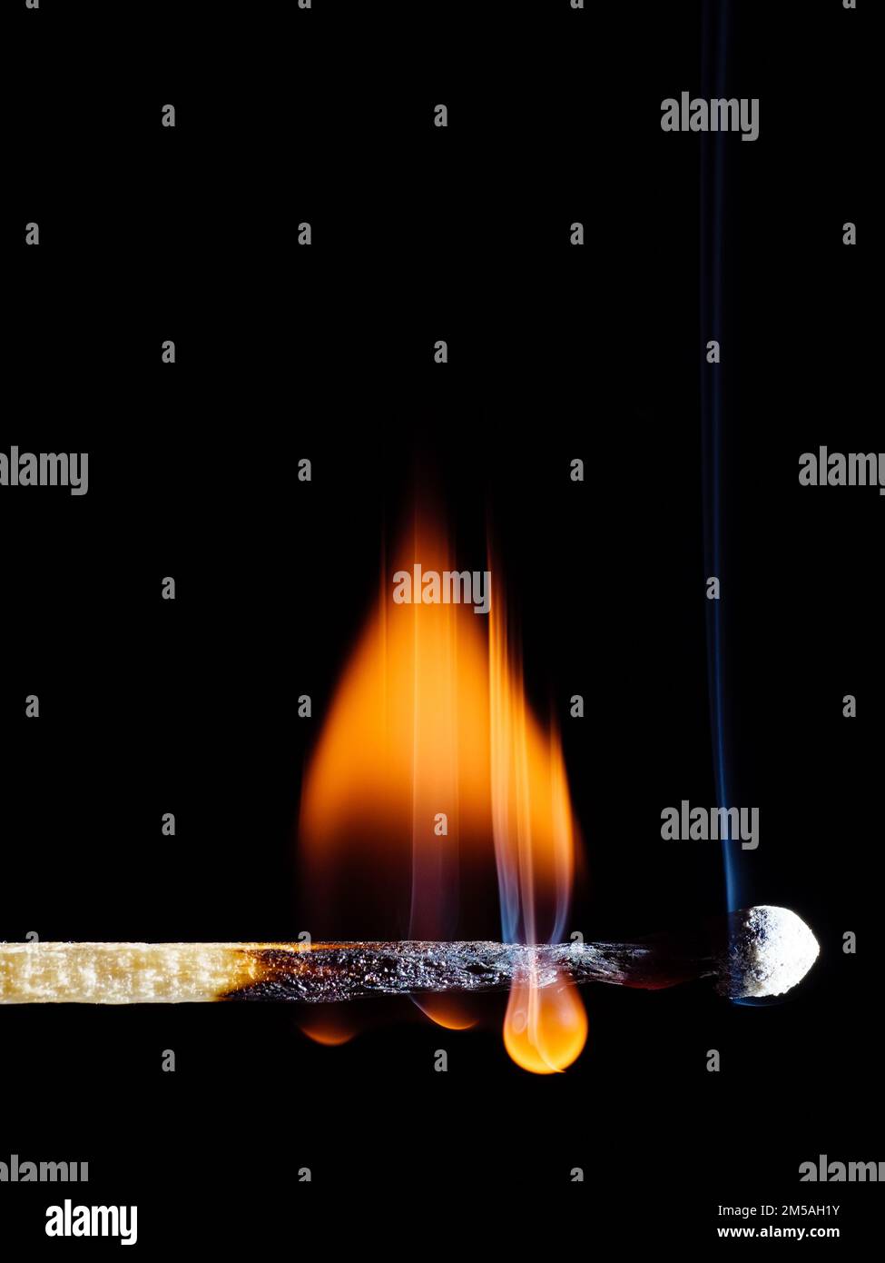 A lit wooden match flaming with an orange flame isolated on black ...