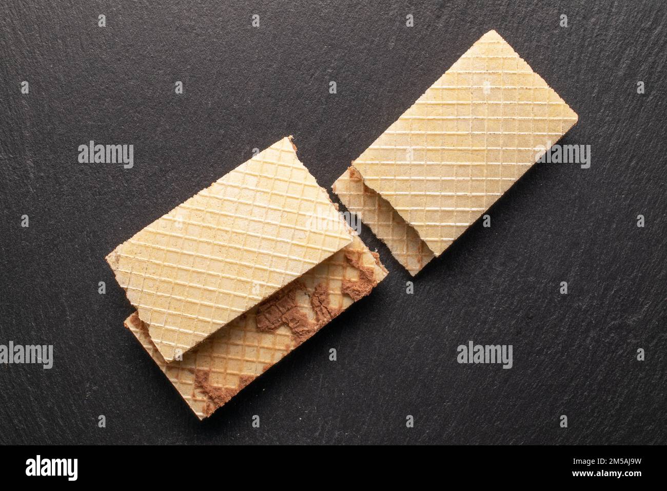 One broken sweet chocolate wafer with white saucer on slate stone ...