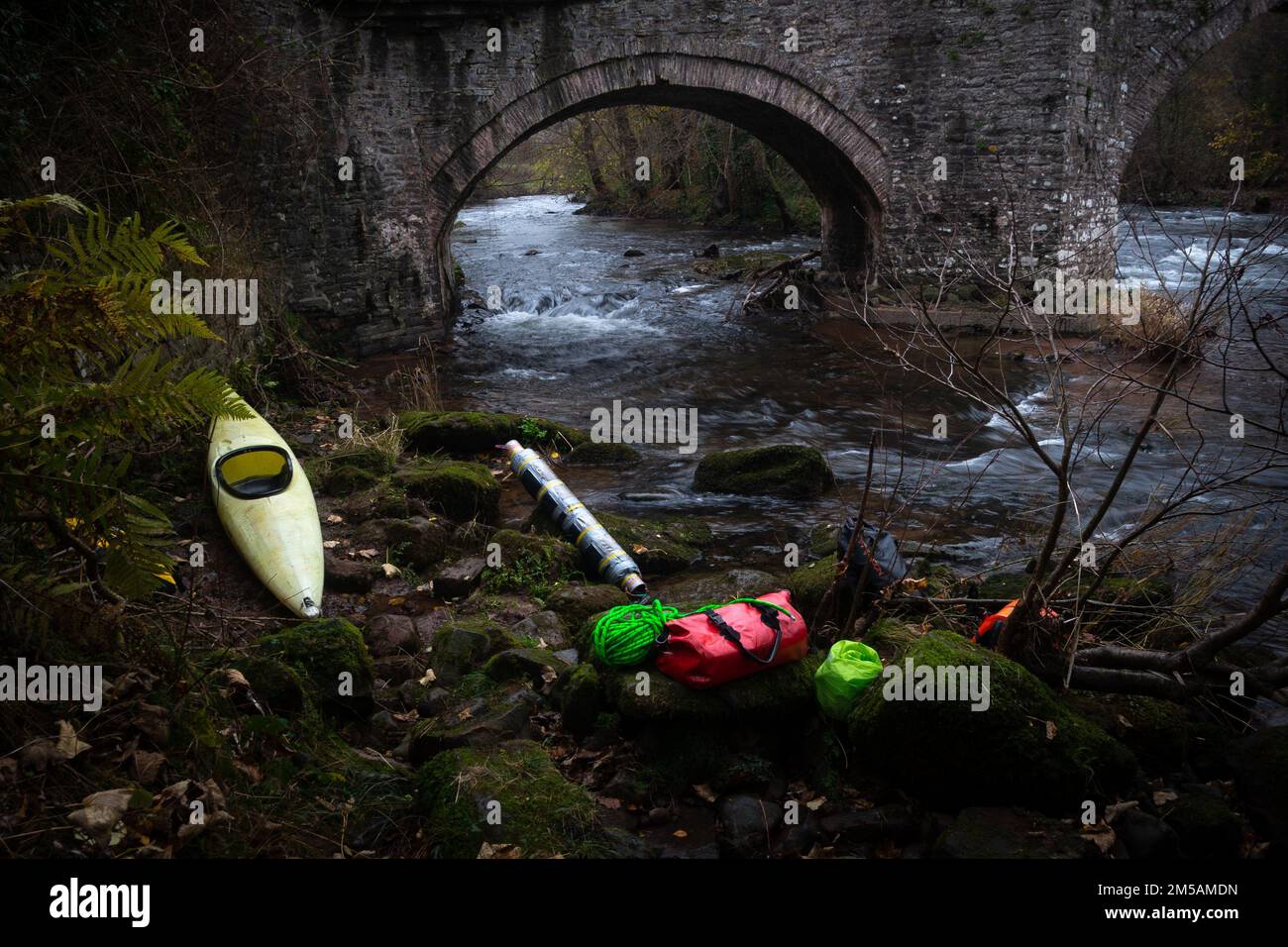 A kayak boat and camping tools on a river bank with ancient stone arch ...
