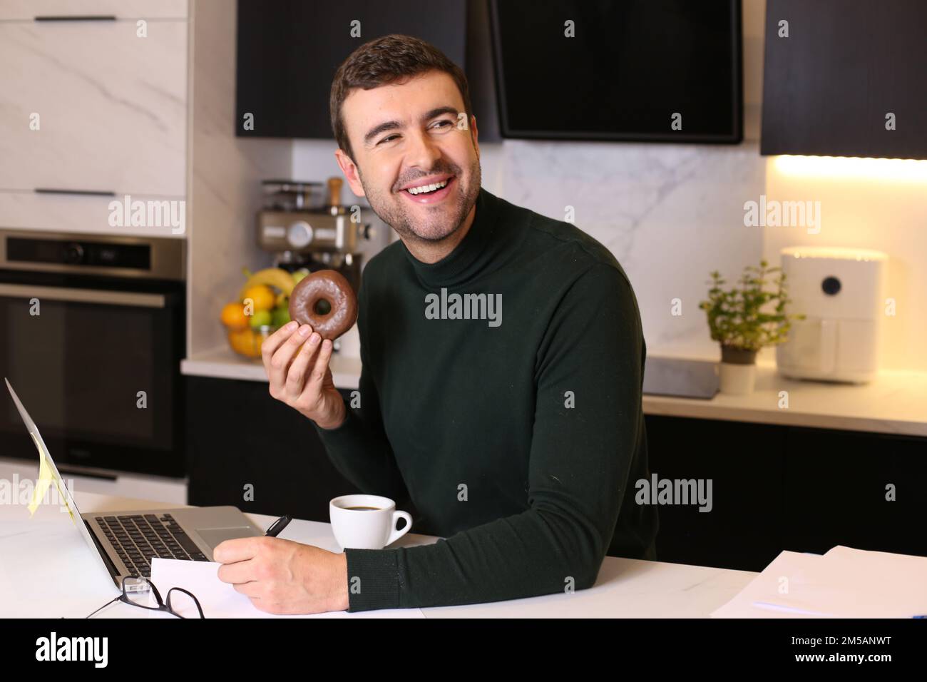 Man eating a doughnut and drinking a coffee in home office Stock Photo ...