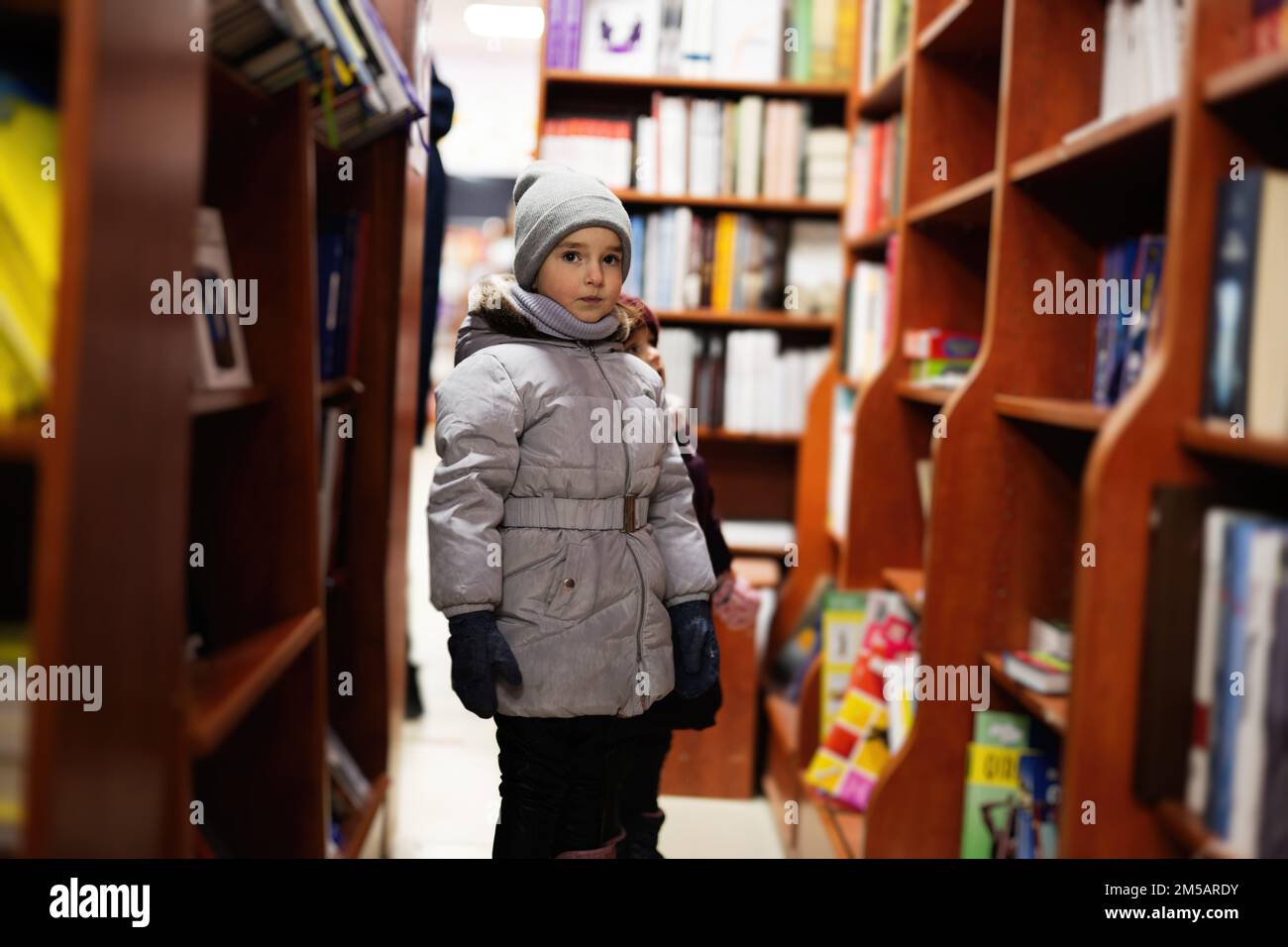 Little cute sisters in jacket reaching a book from bookshelf at the ...