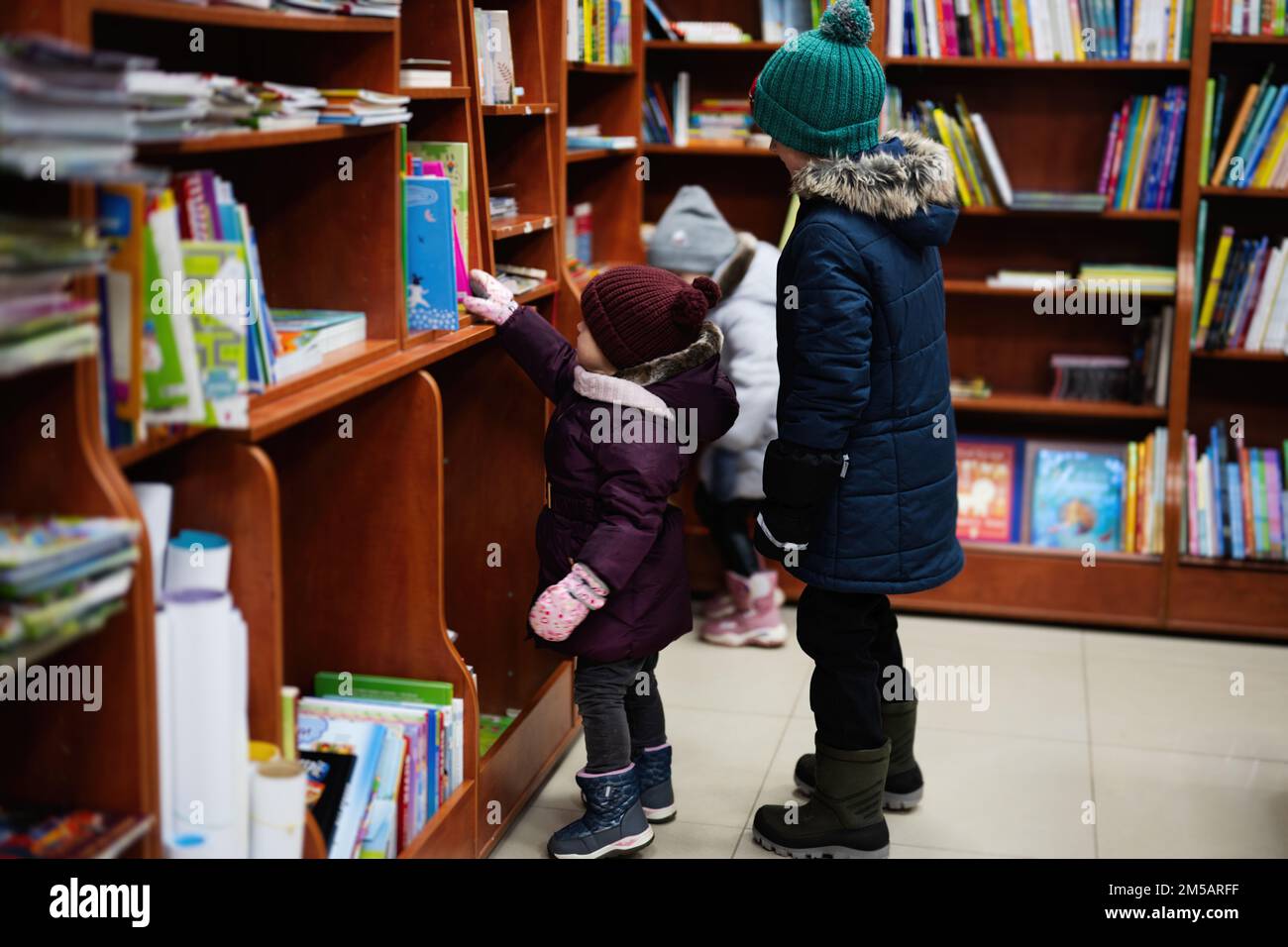 Little cute baby in jacket reaching a book from bookshelf at the ...