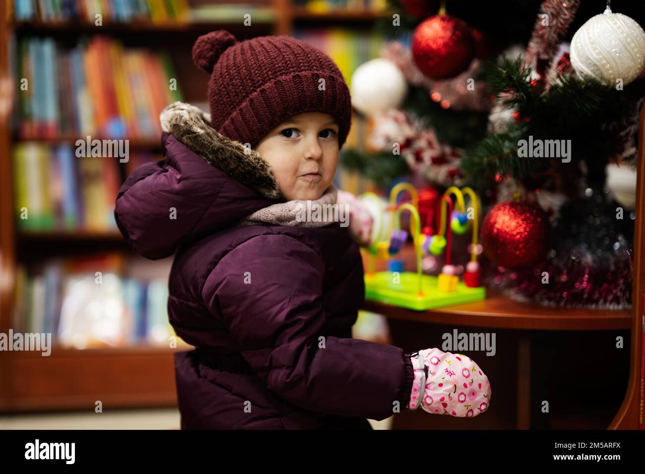Little cute baby in jacket reaching a book from bookshelf at the ...
