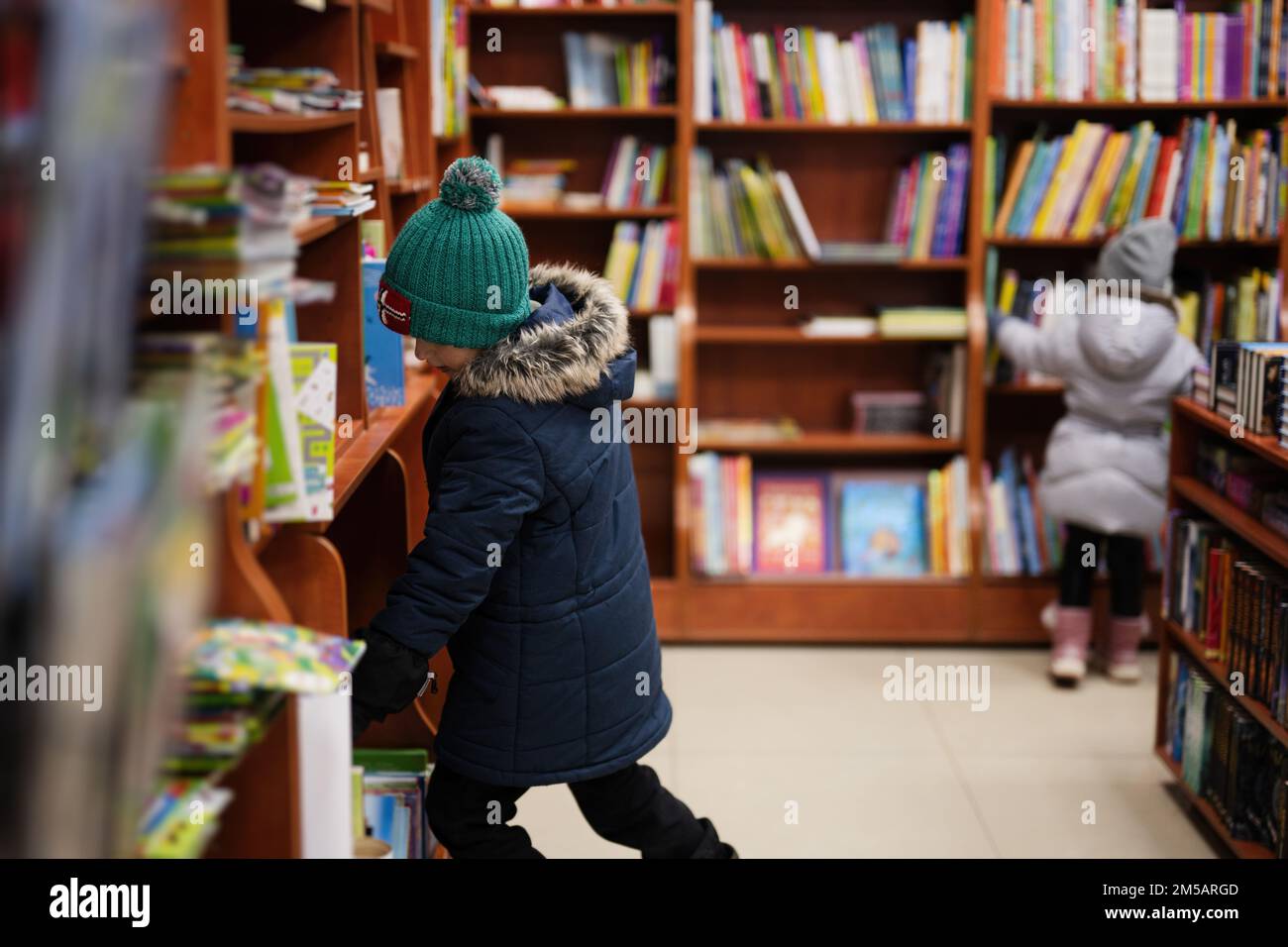 Boy in jacket reaching a book from bookshelf at the library. Learning ...