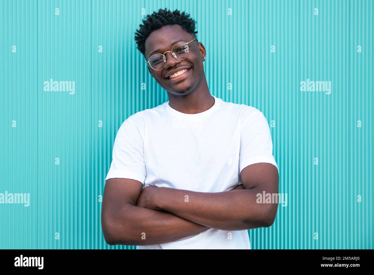 Happy young african american man smiling with arms crossed on turquoise ...