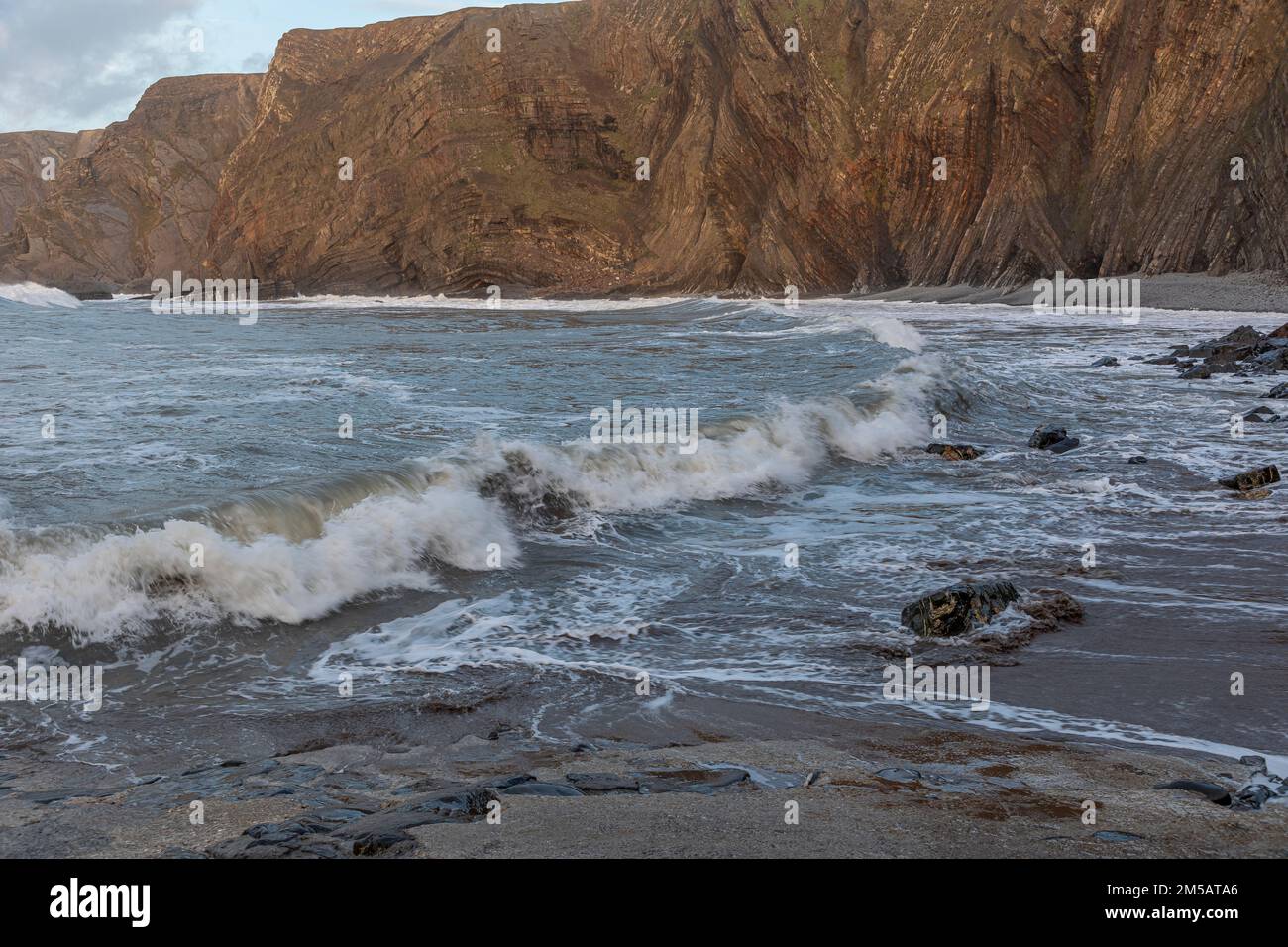 beautiful unique cliffs in the sunshine with a large wave coming into ...