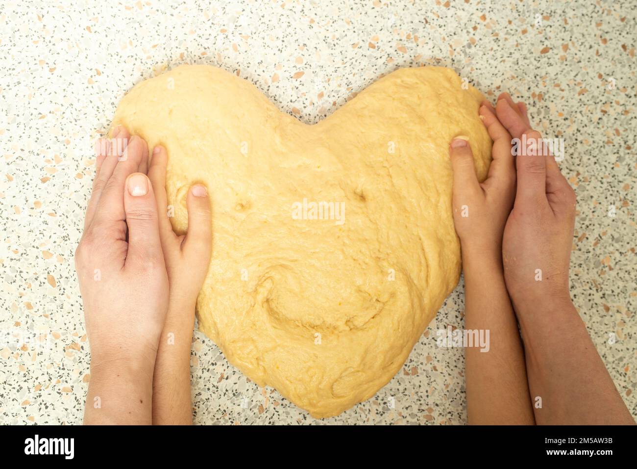 Mother and son hands holding dough in the shape of a heart with a ...