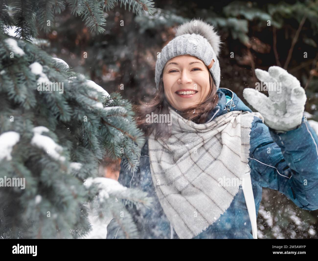 Smiling woman in cable knitted hat is playing with snow. Fun in park ...