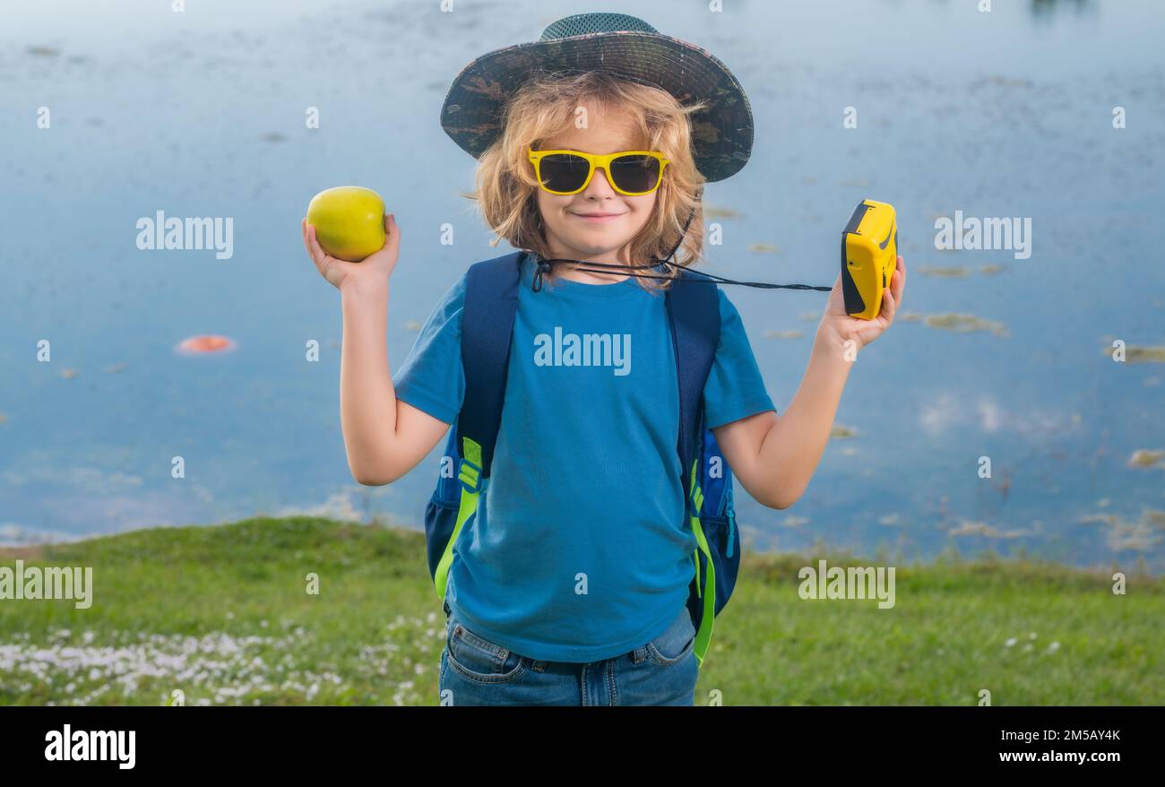 Cute blond kid with camera wearing explorer hat and backpack on nature ...