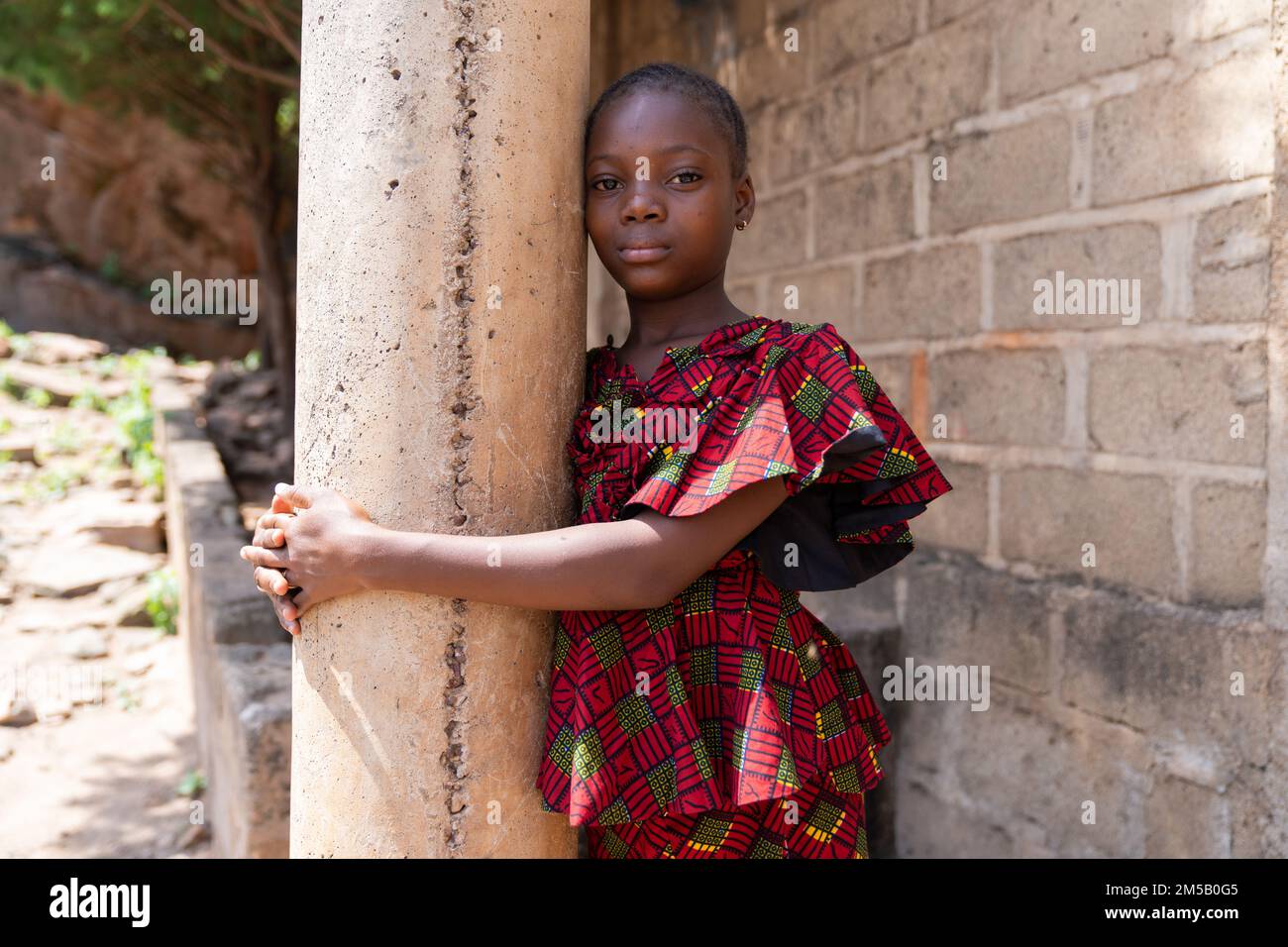 Pretty young African girl hugging a concrete pole with a contemplative ...