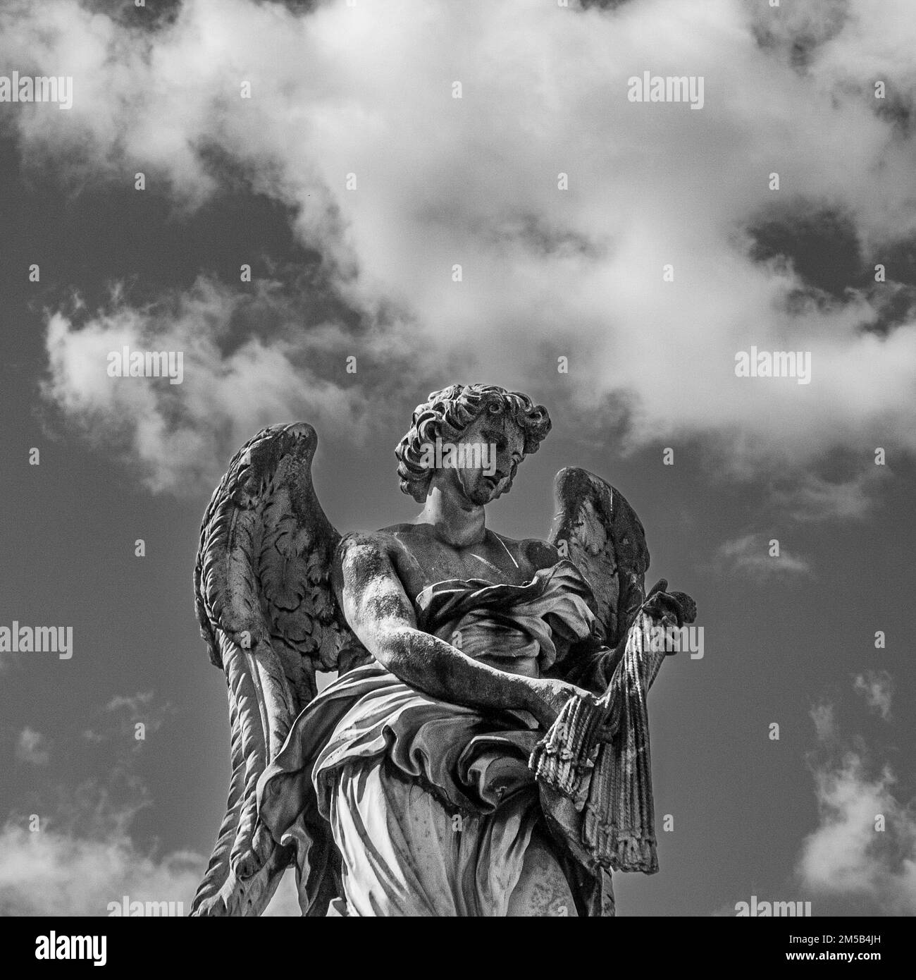 A grayscale of an angel statue against the daytime sky and clouds Stock ...
