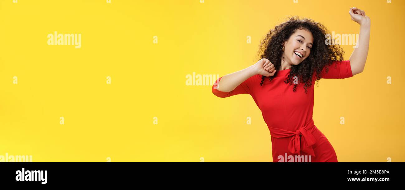 Carefree girl feeling uplifted and joyful dancing in red dress raising ...