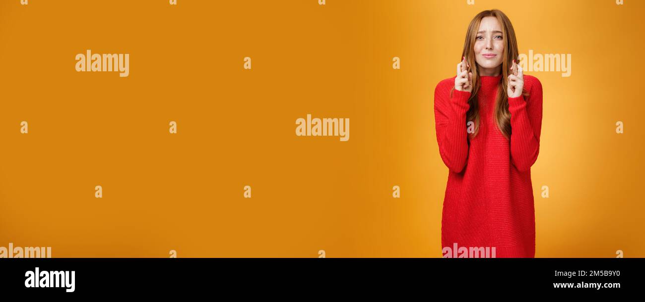 Hopeful worried redhead girl in red sweater frowning pursing lips cross ...