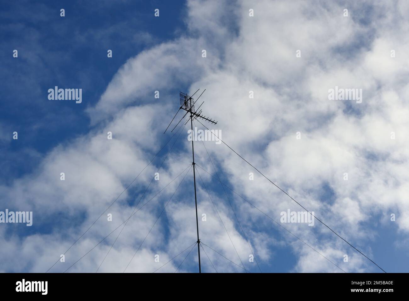 A low angle of an antenna with wires against the blue sky and floating ...