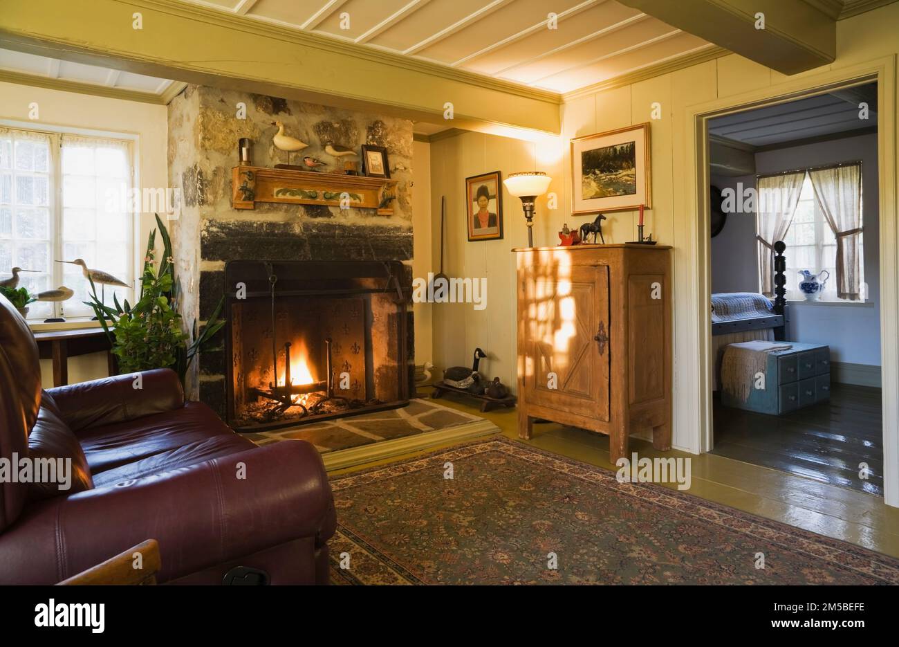 Burgundy leather sofa with lit stone fireplace and small wooden antique ...