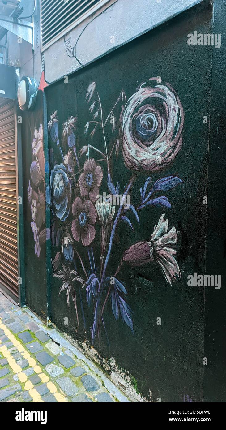 A vertical shot of small street with art graffiti flowers on a wall in ...