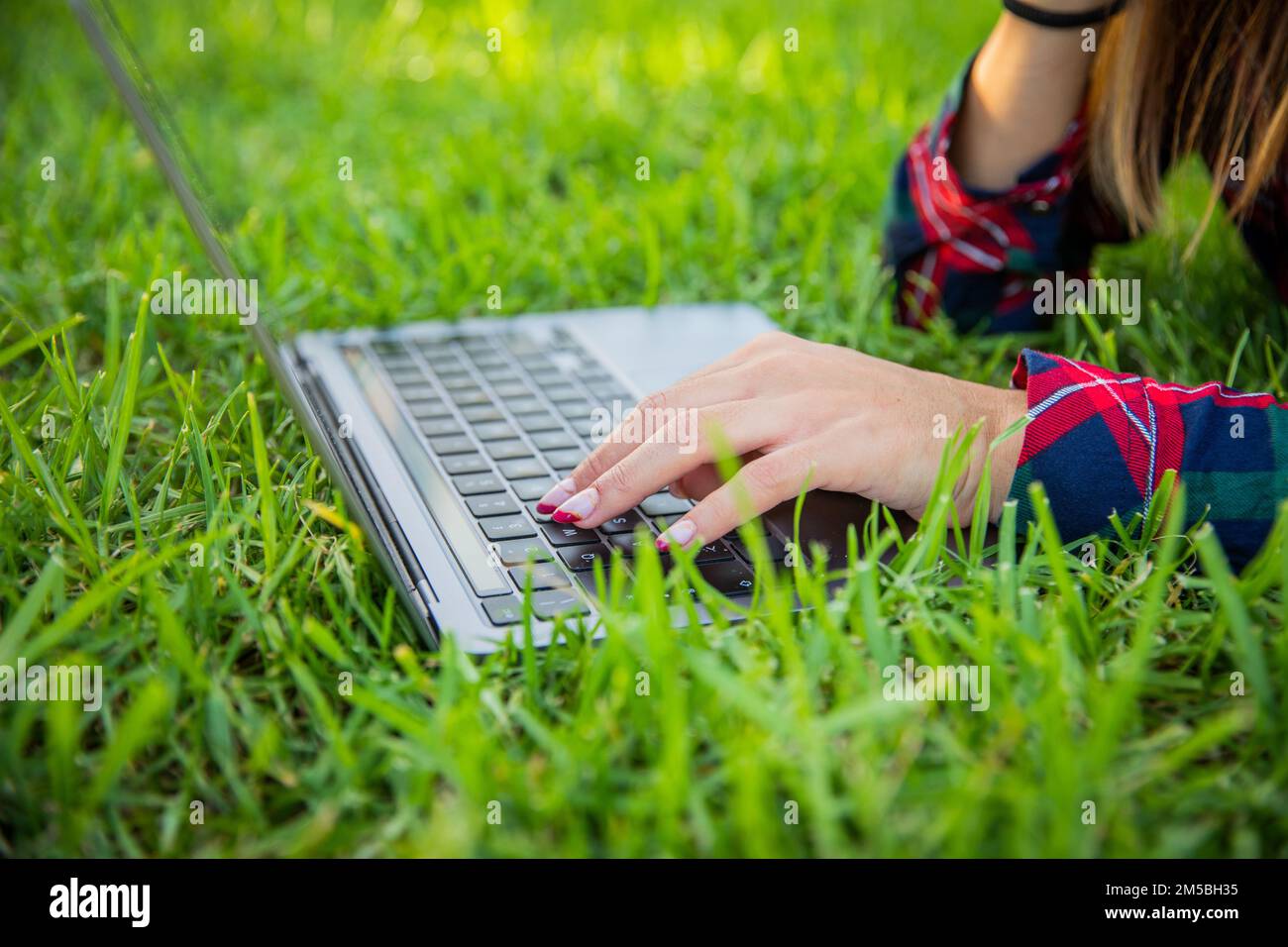 Close-up of a girl's hands typing with laptop resting on a meadow ...