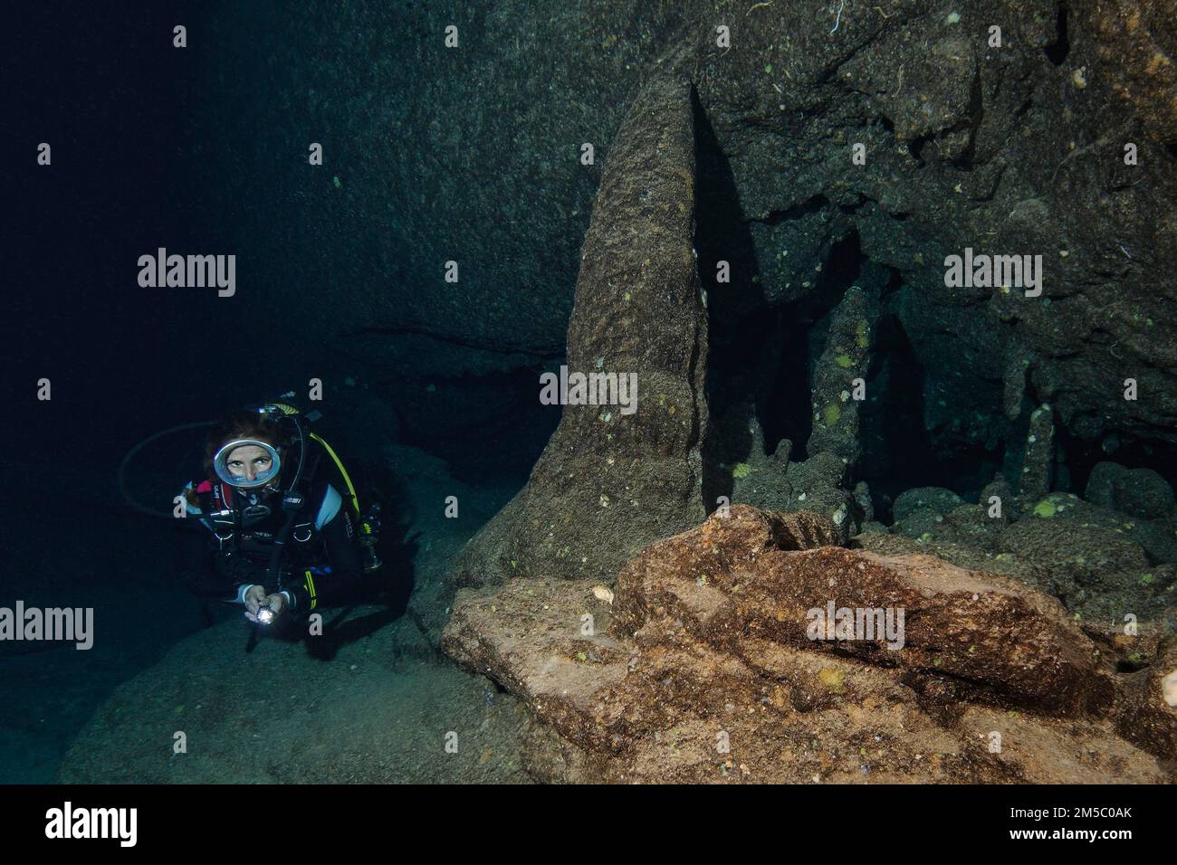Diver swims diving through underwater cave with stalactites weathered ...