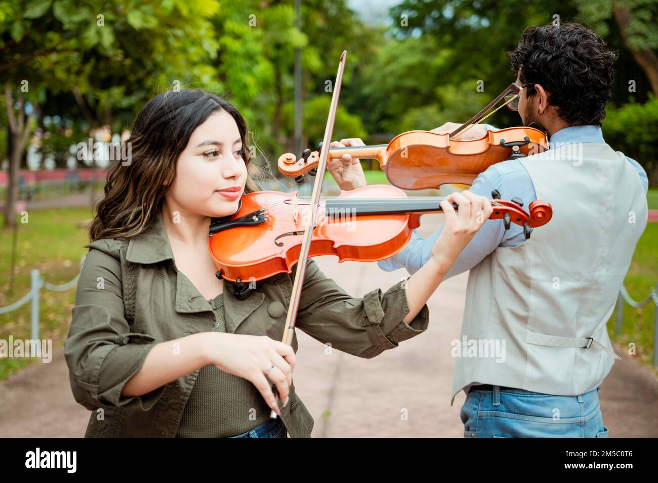 Two young violinists standing playing violin in a park. Portrait of man ...