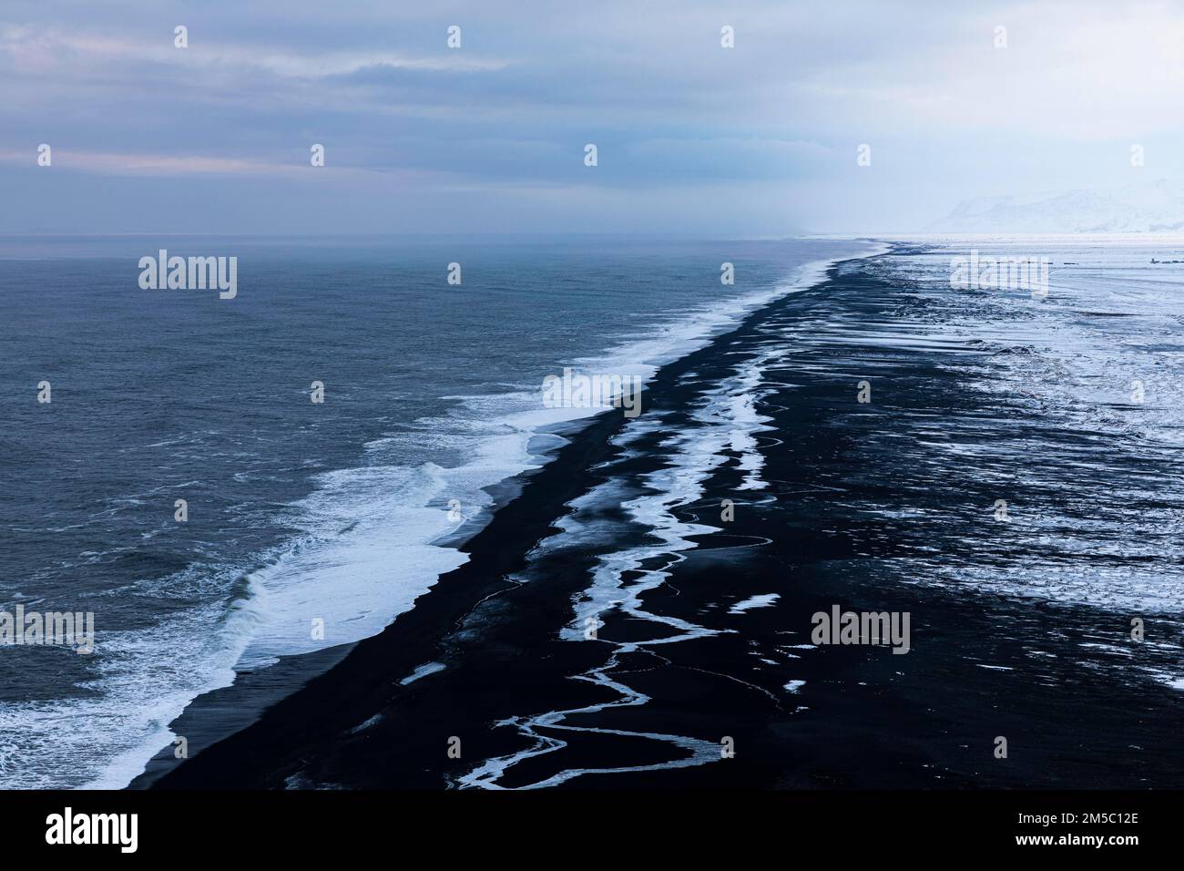 Foamy white waves and icy surfaces on the black pebble beach ...