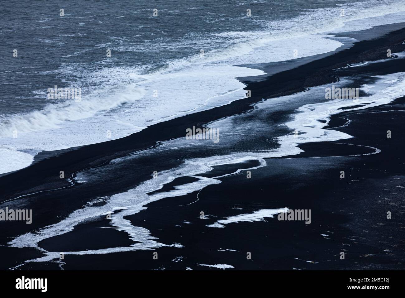 Foamy white waves and icy surfaces on the black pebble beach ...