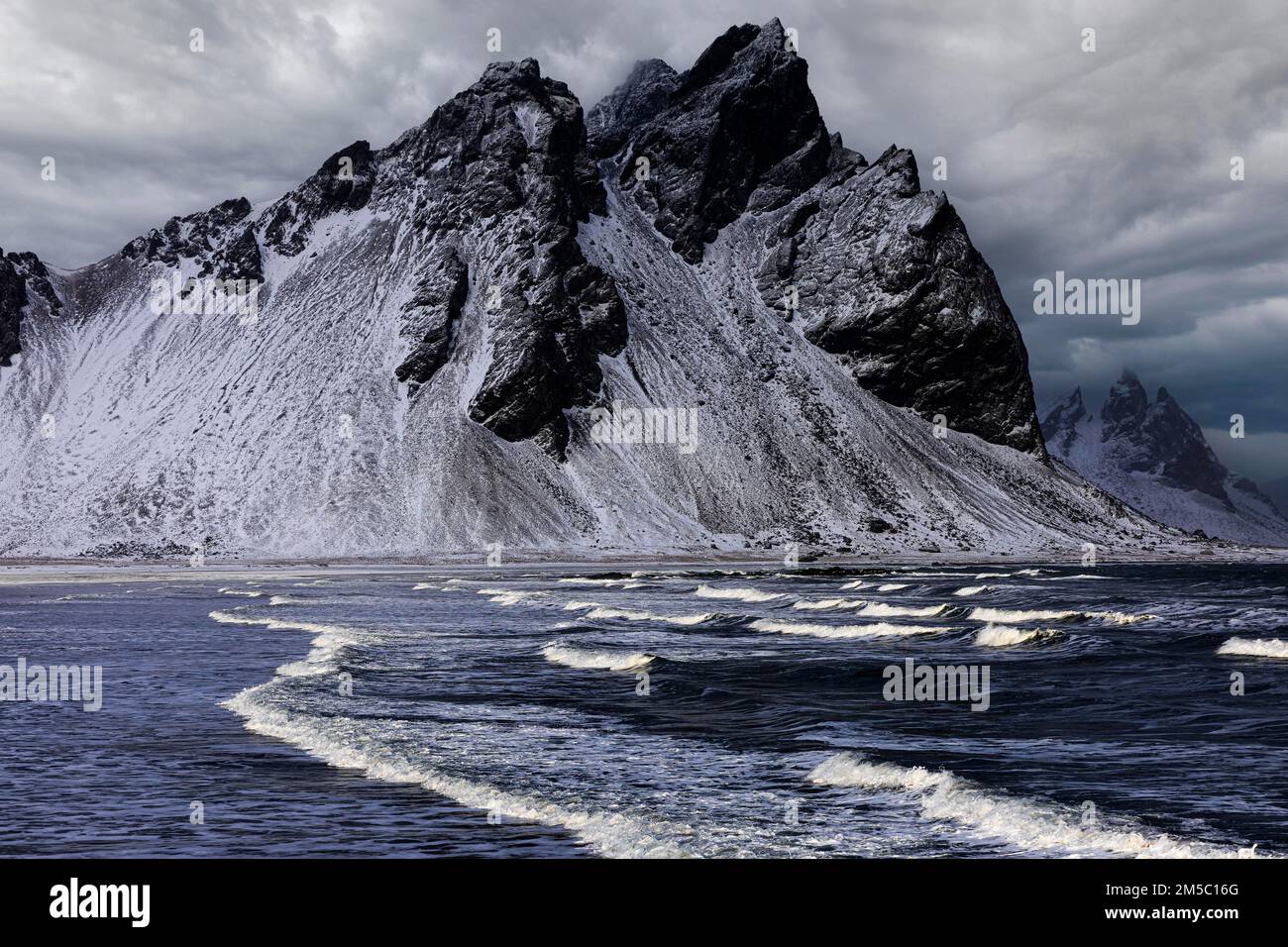 White foamy waves on the beach of Stokkness, behind snowy rocky slopes ...