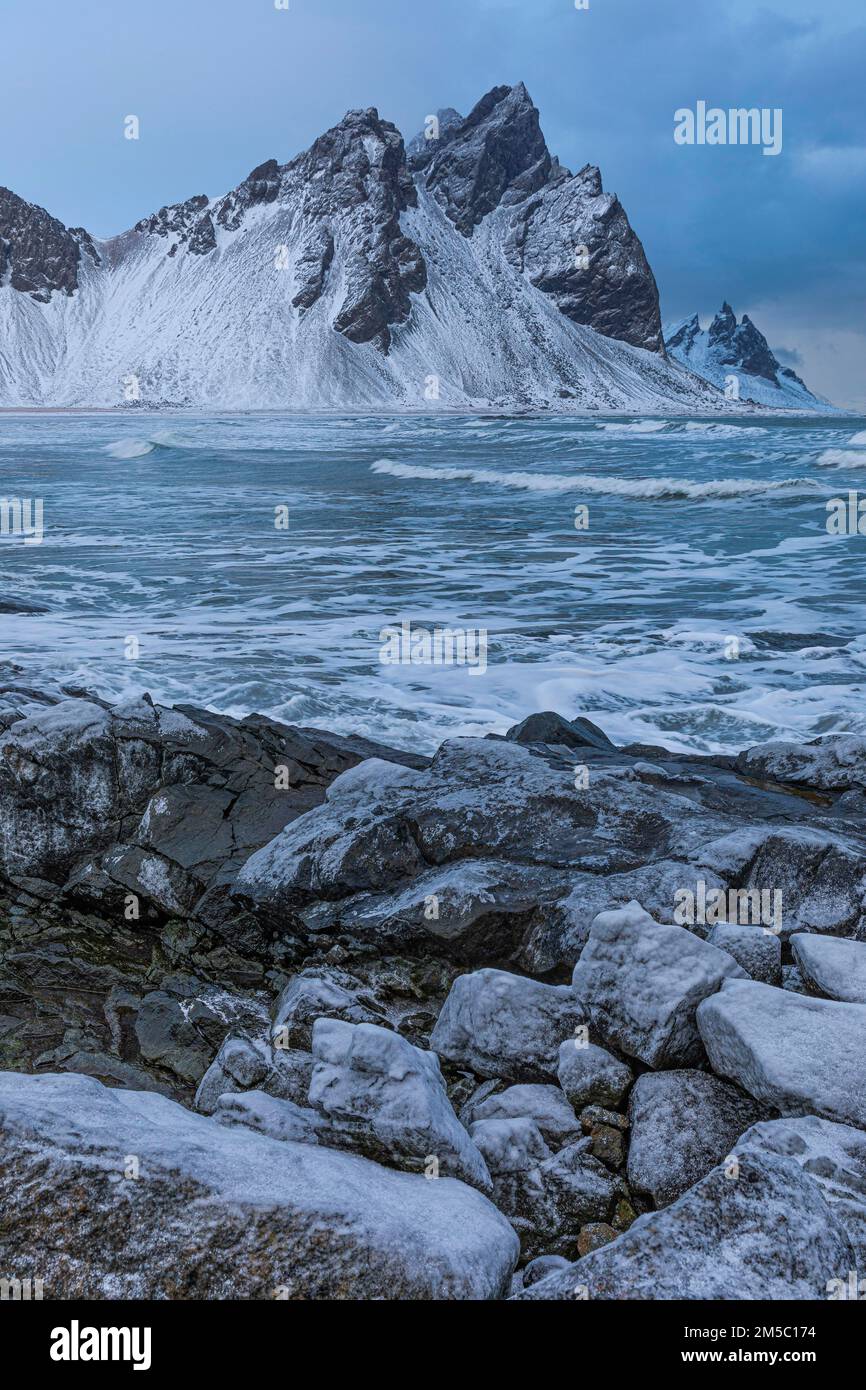 Iced rocks on the beach of Stokkness, behind them the snowy rocky ...