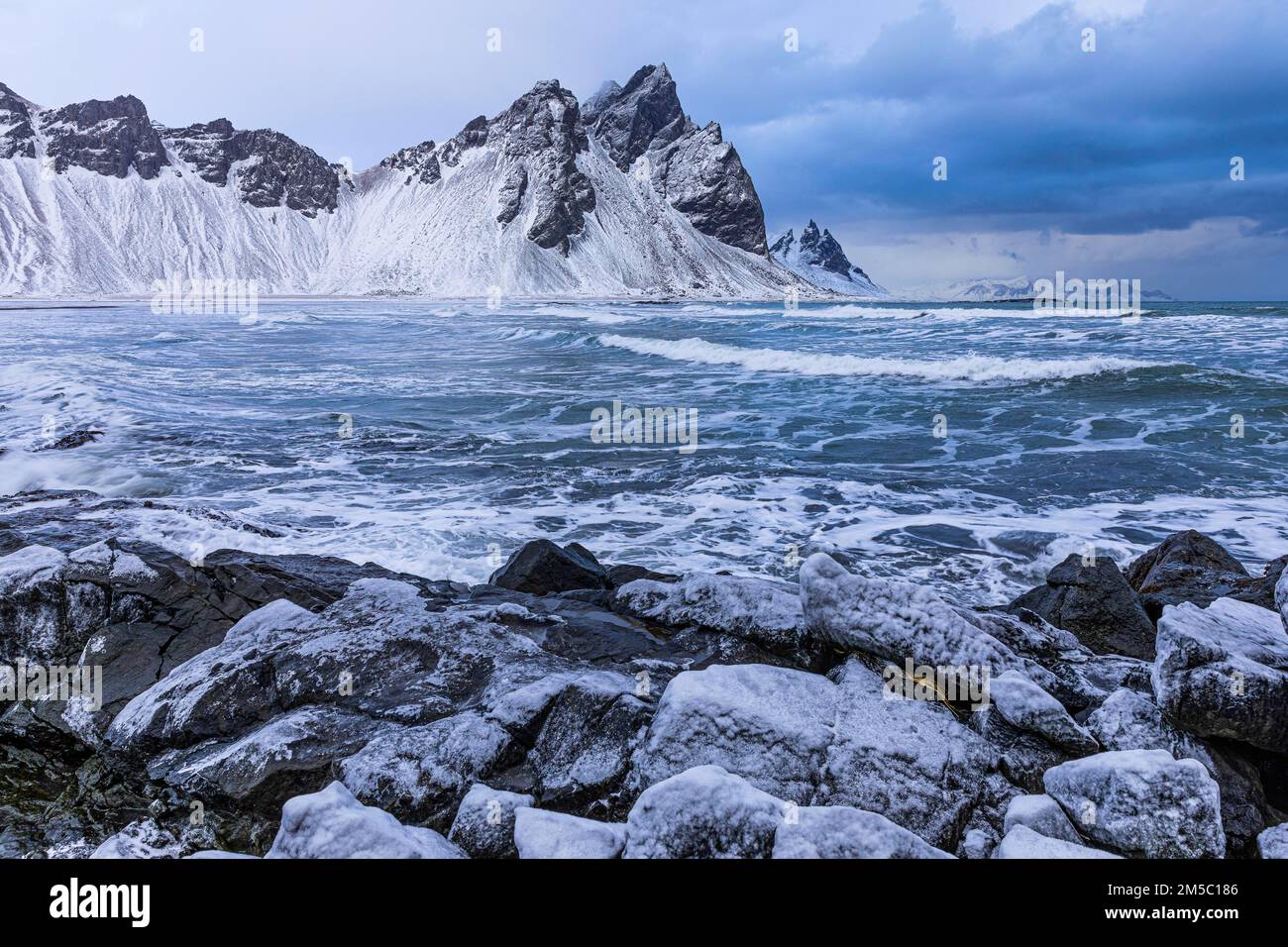Iced rocks on the beach of Stokkness, behind them the snowy rocky ...