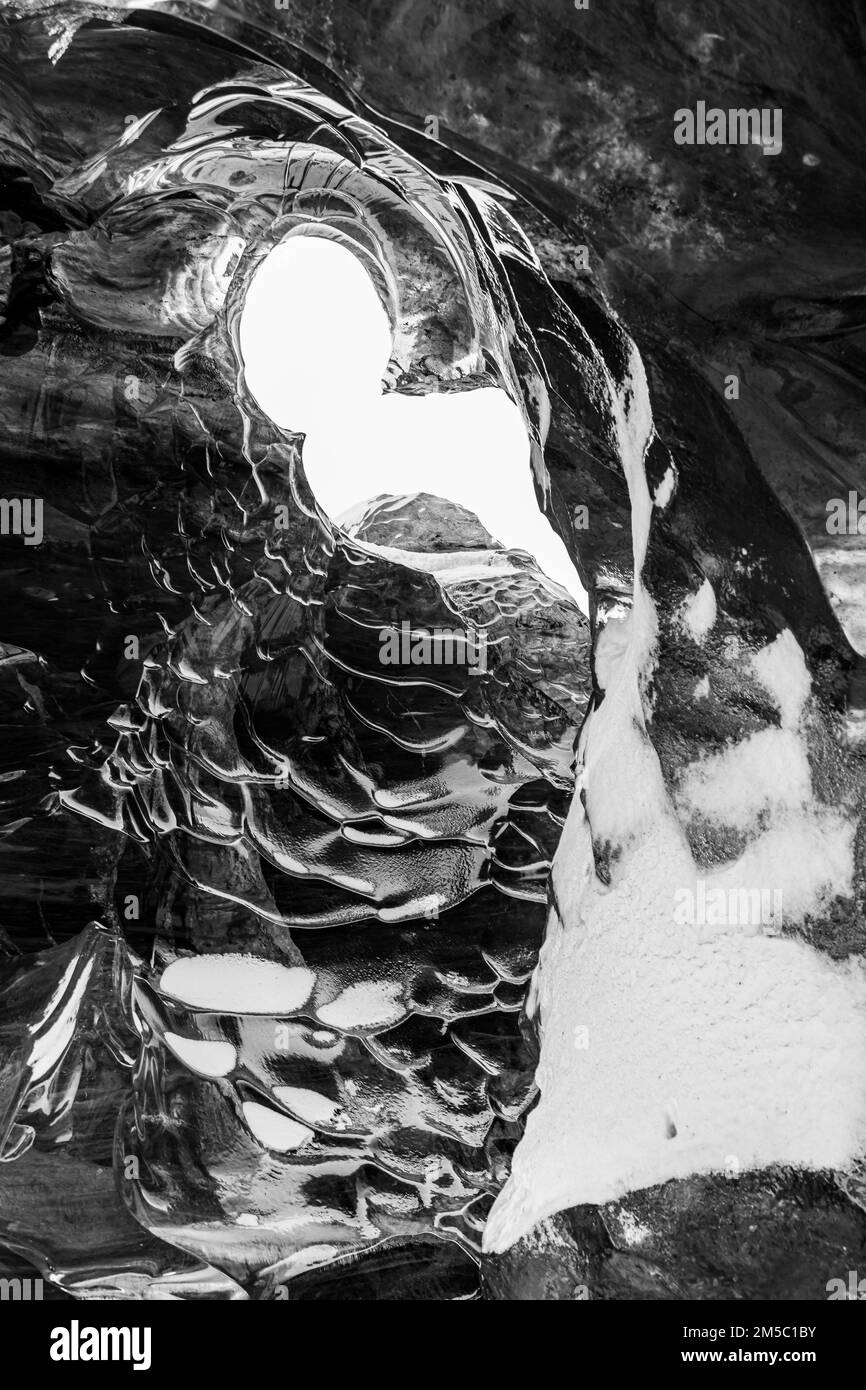 Ice cave open to the top with snow-covered ice combs, black and white ...