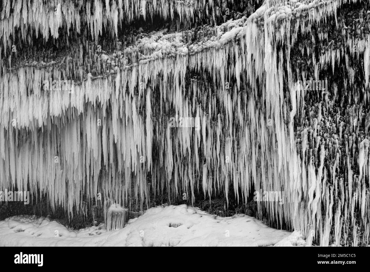 Icicles on the rock face at Skogafoss waterfall, black and white photo ...
