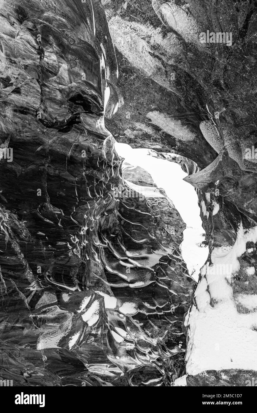 Ice cave open to the top with snow-covered ice combs, black and white ...